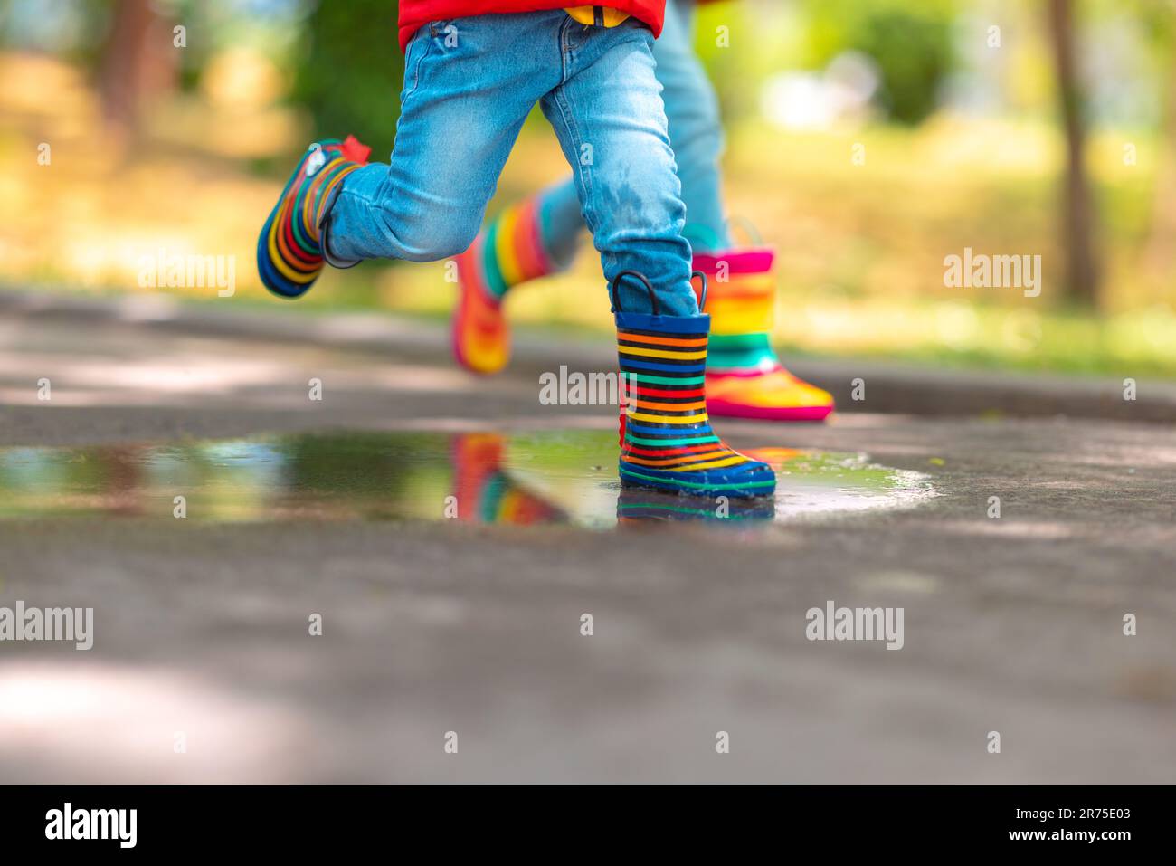 Feet of child in colorful rubber rain boots jumping over rainy puddle ...