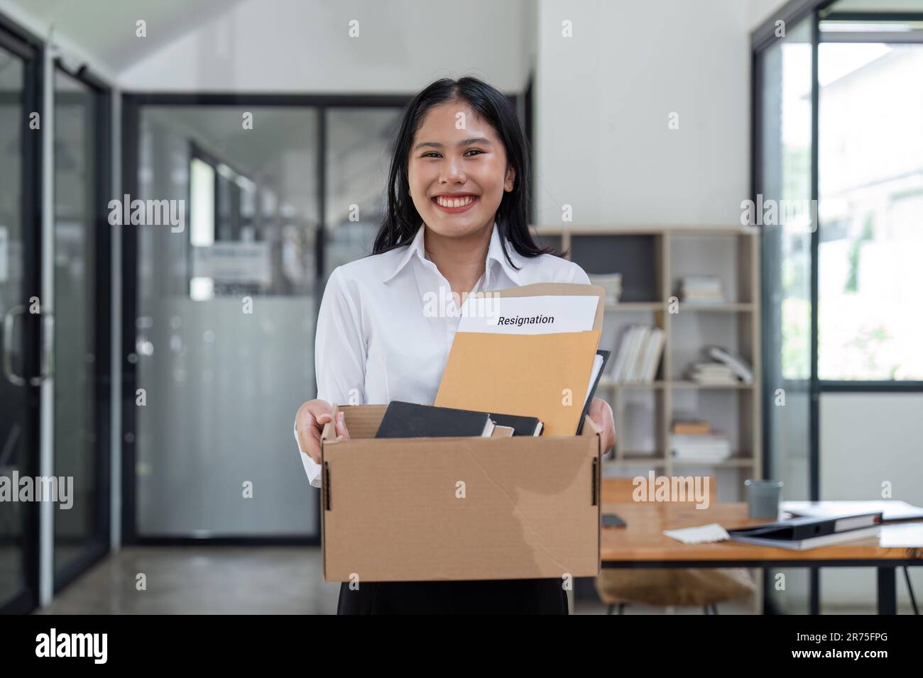 Smiling young Asian female office worker her resignation, carrying her personal stuff, happy to ...