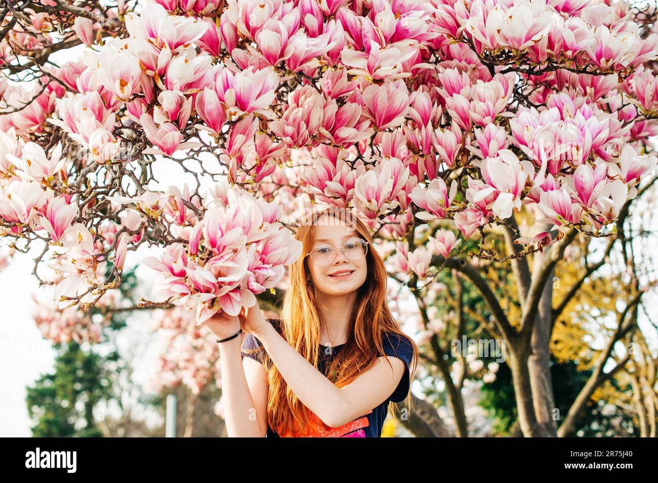 Spring portrait of adorable red-haired preteen kid girl with magnolia ...