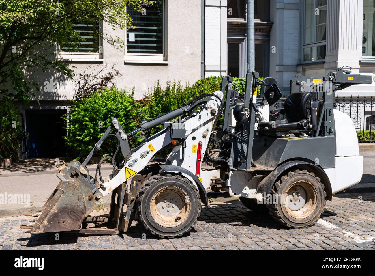 A small white excavator standing on the sidewalk near the entrance to a ...