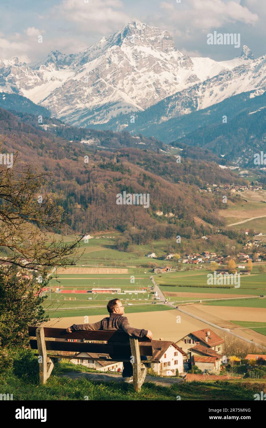 Man relaxing on the bench, admiring swiss Alps in canton of Valais ...
