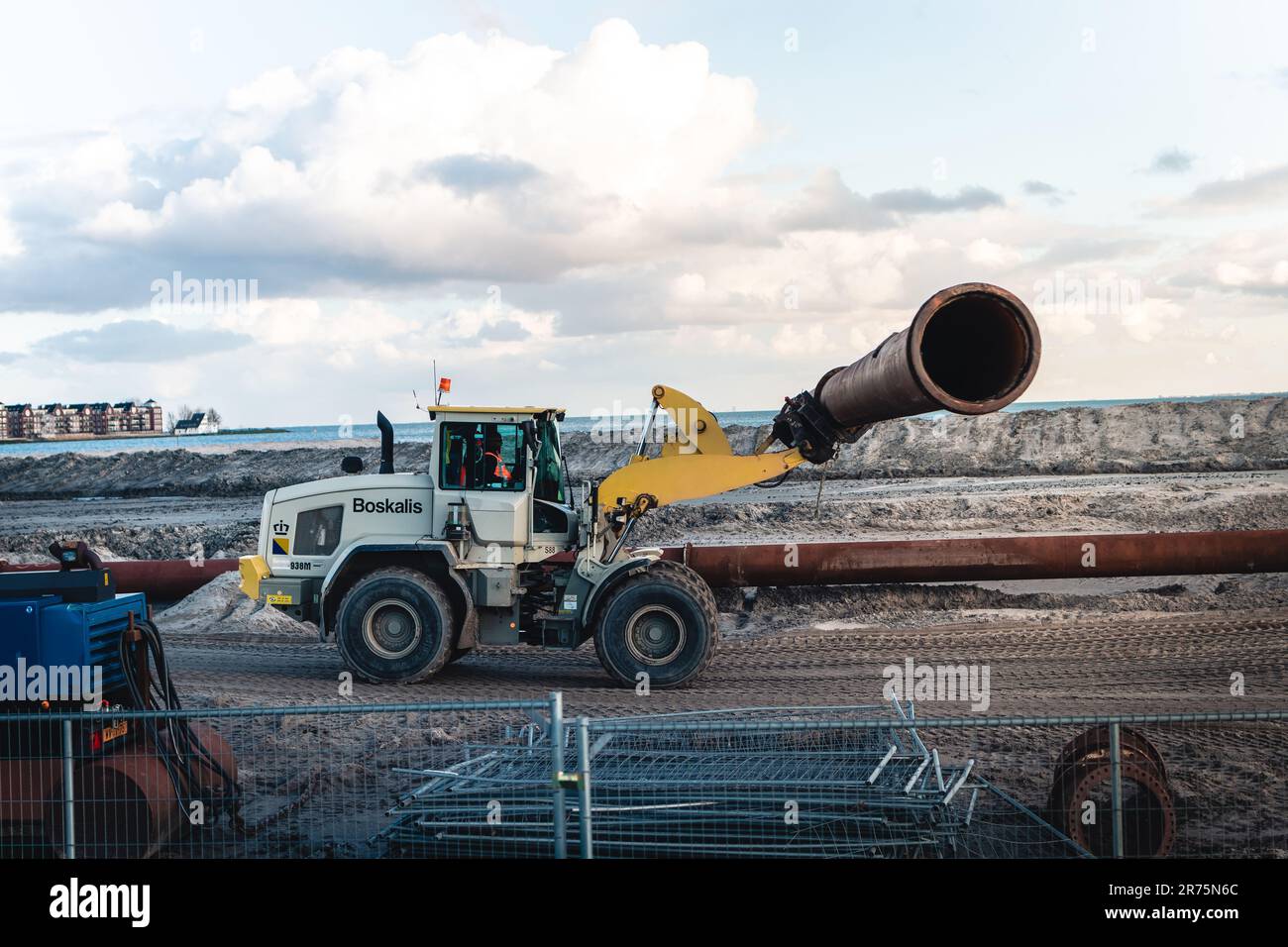 A yellow construction vehicle with a wheeled arm is pulling a large cylindrical tube out of the ...