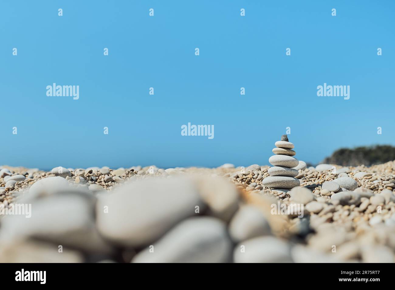 Pyramid stones balance on the beach against a blue bright sky. Object ...