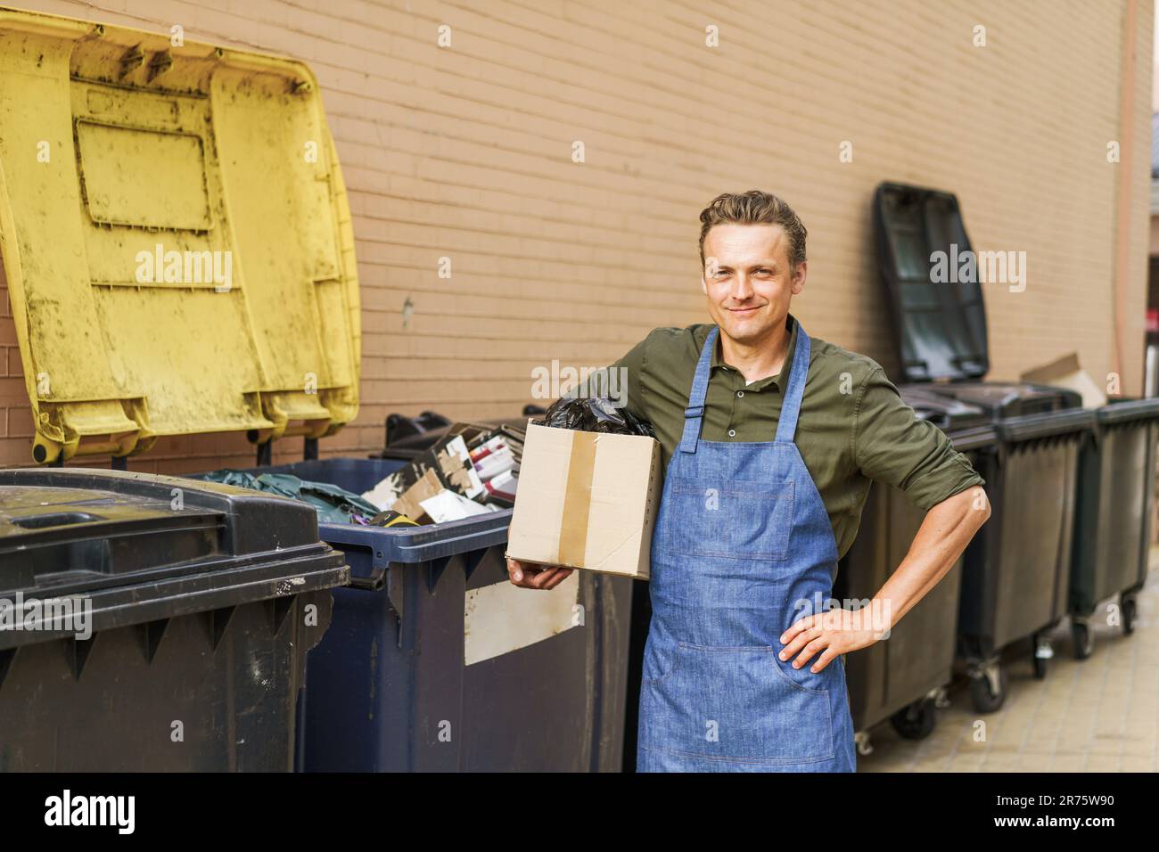Garbage sorting with blond smiling man wearing blue apron. Man holds ...