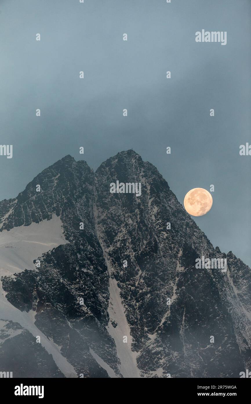 Full moon rolls down next to Großglockner summit, foggy, summit cross ...
