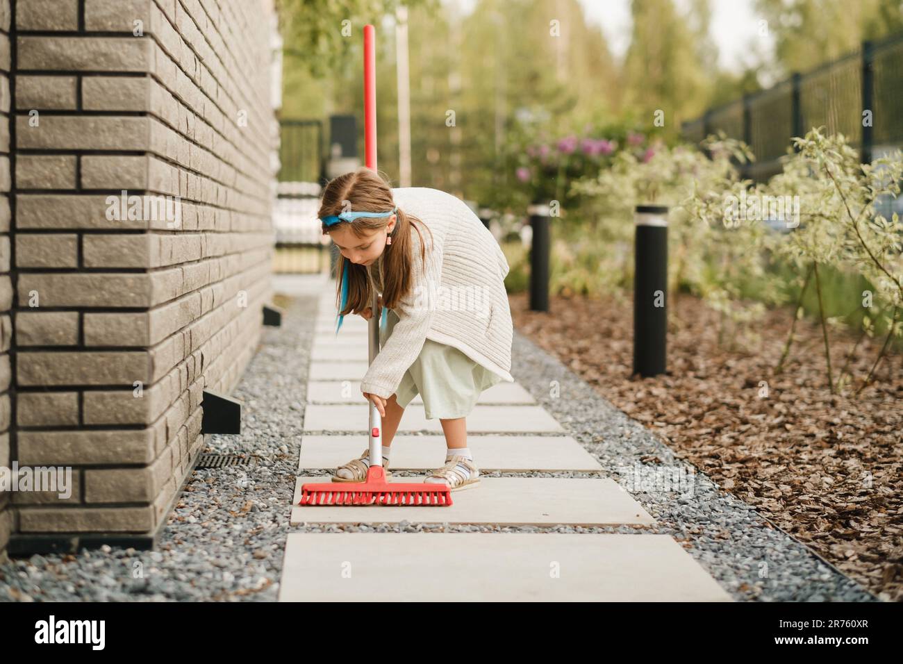 A little girl with a brush cleans a path on the street in the courtyard ...