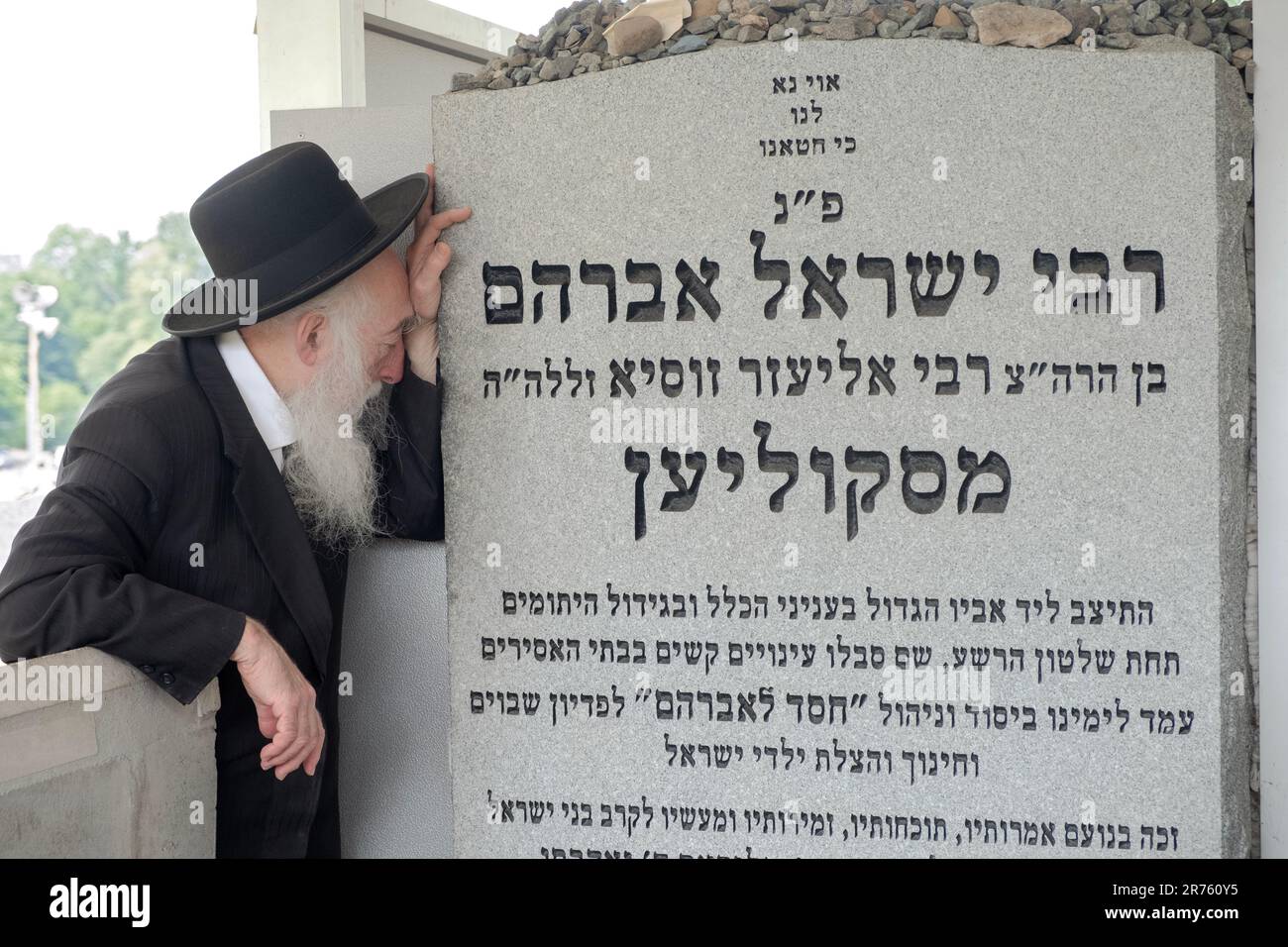 An older Jewish man engages in fervent prayer near the headstone of a ...