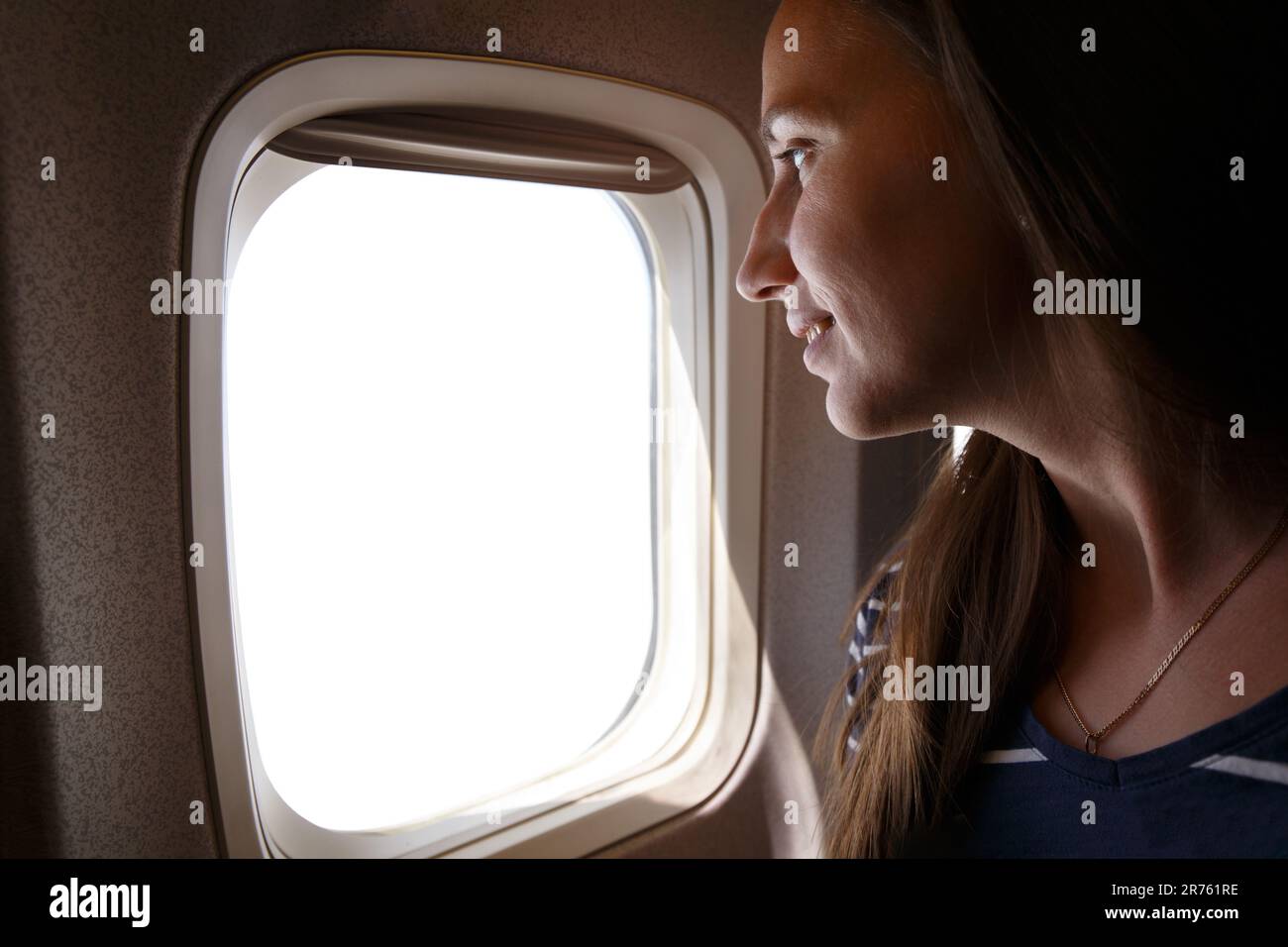 Young smiling woman looking through the plane window with white space ...