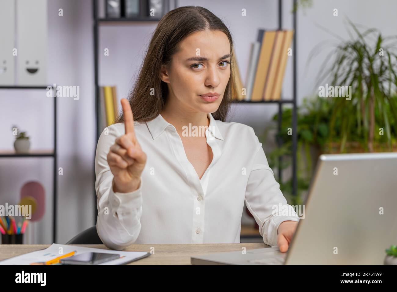 Caucasian young business woman working on laptop computer shakes finger ...