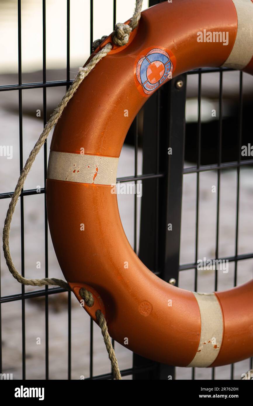 A vibrant orange life preserver is securely attached to a black metal ...