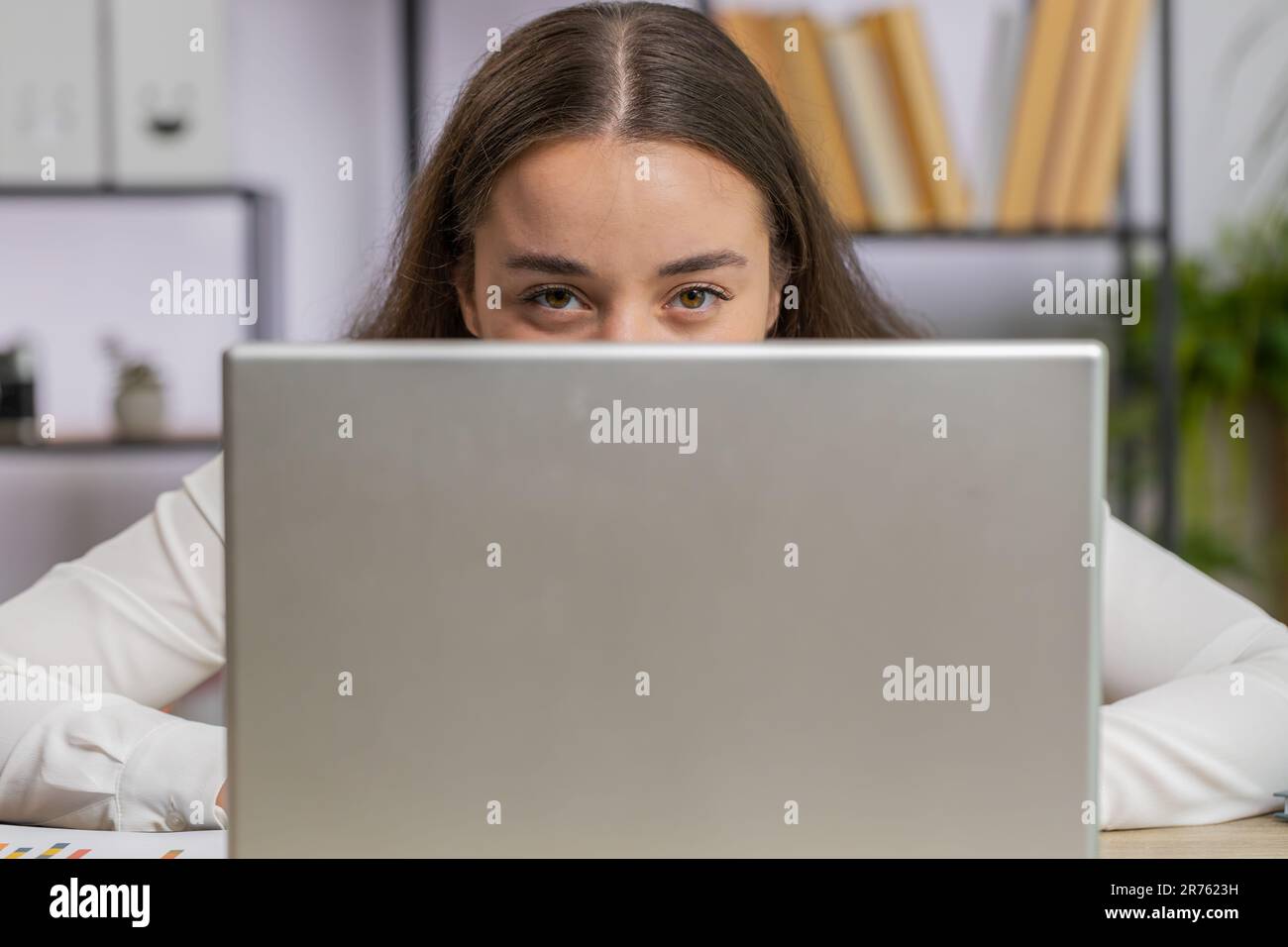 Confident business woman hiding behind laptop computer, looking at ...