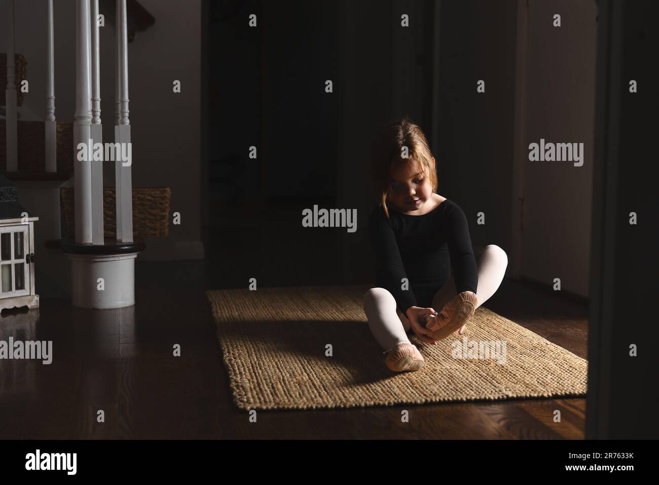A young girl in a ballet leotard and tights sits in a doorway and ...