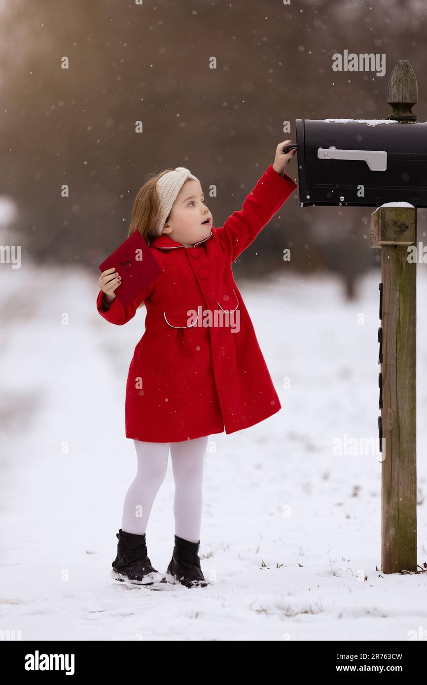 A young girl stands on the side of a snowy road and stretches up to ...