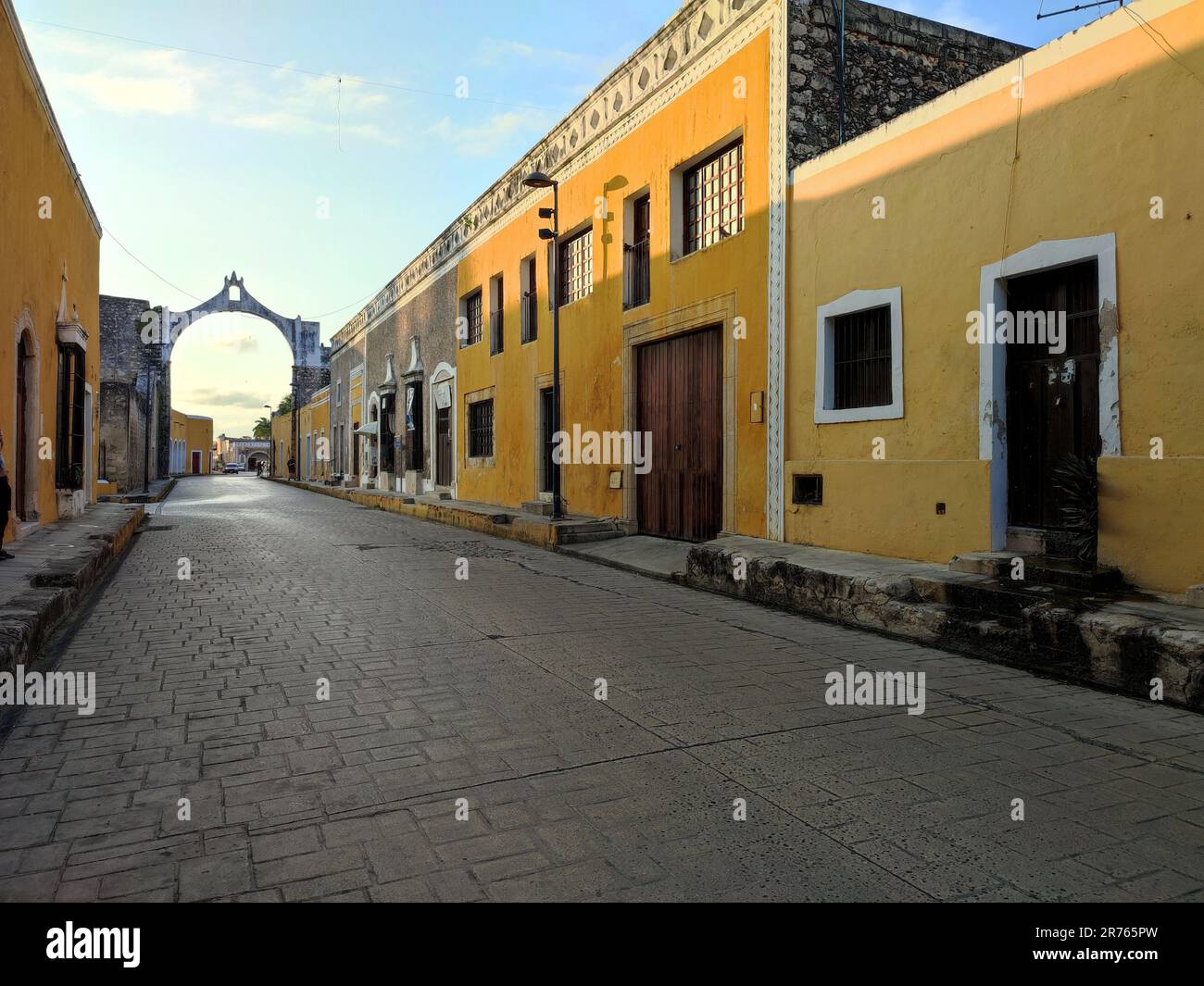 A view of a cobbled street in a Mexican town, with old yellow buildings ...