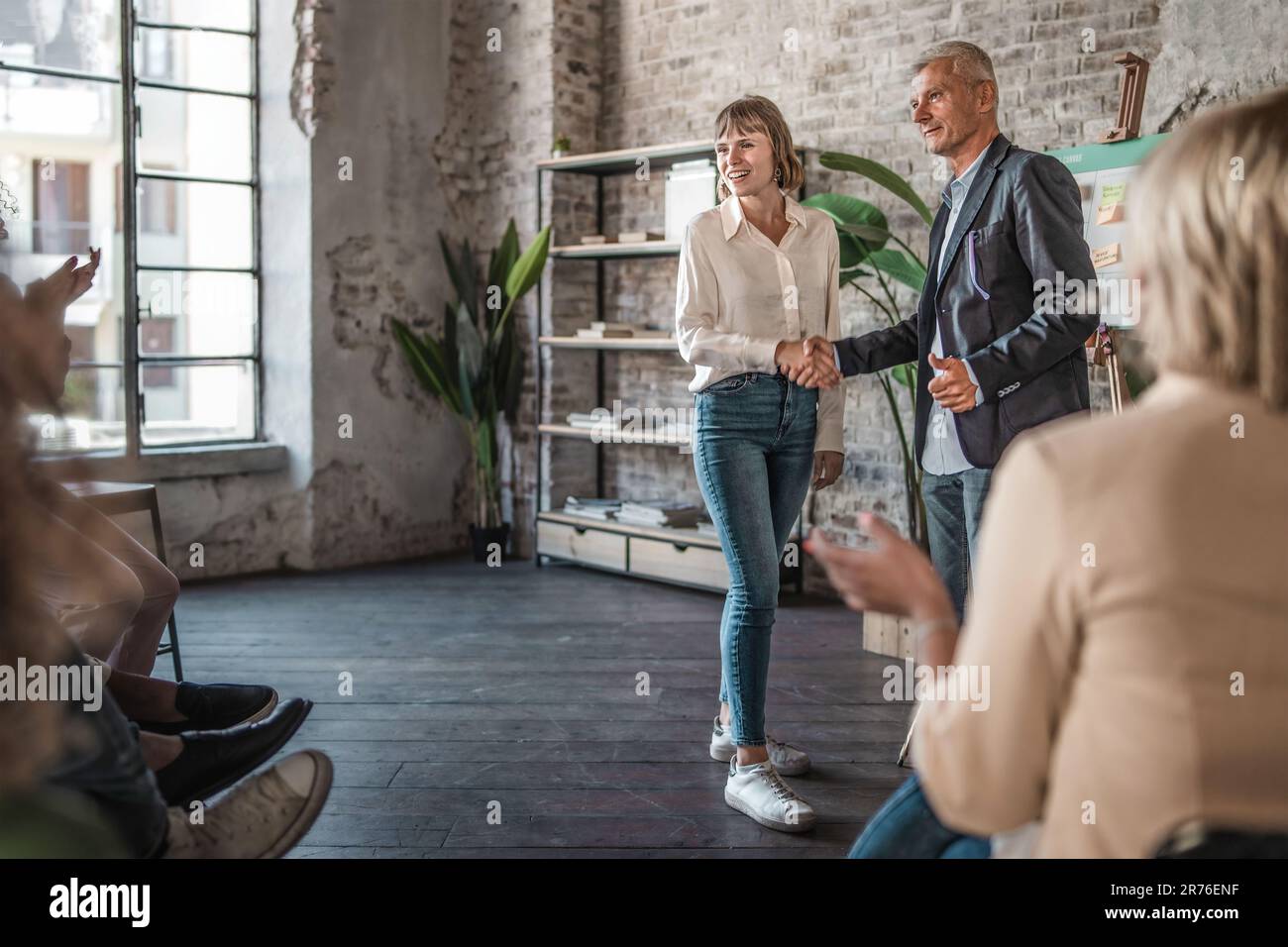A young Caucasian woman and a man shake hands with smiles while their ...