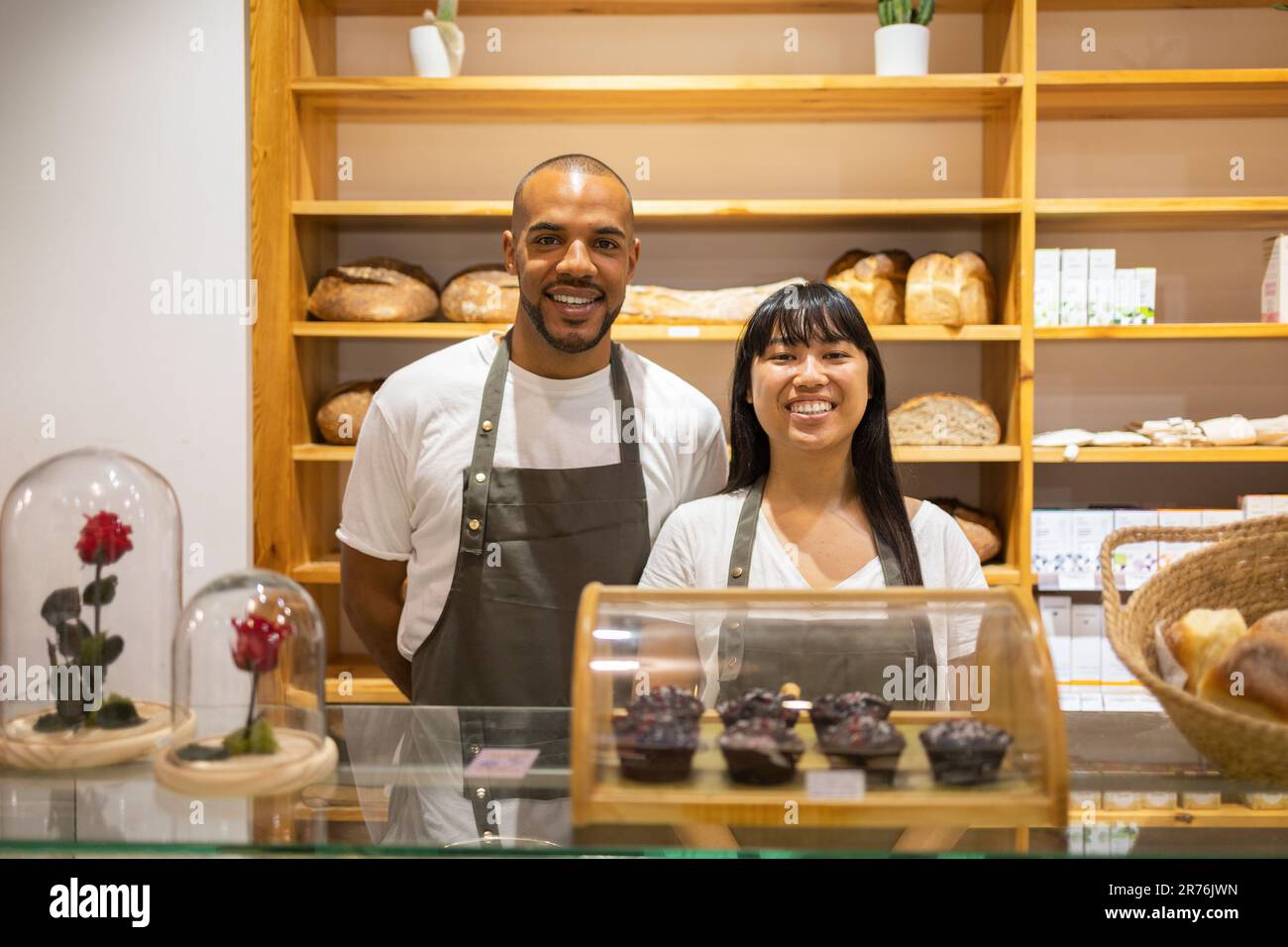 Positive young multiracial coworkers in aprons smiling and looking at ...