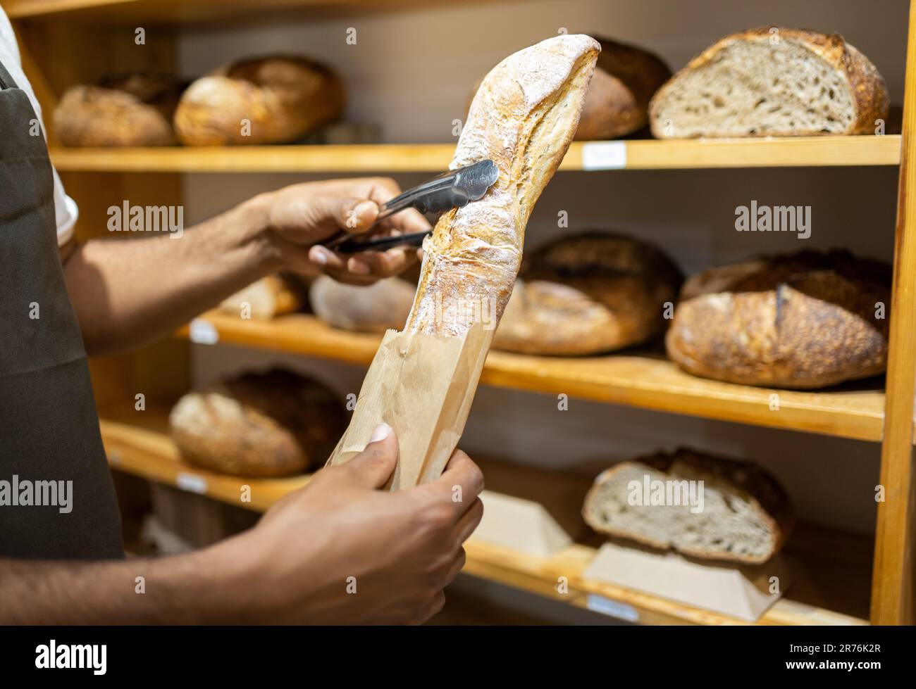 Anonymous cropped African American male seller in apron putting fresh ...