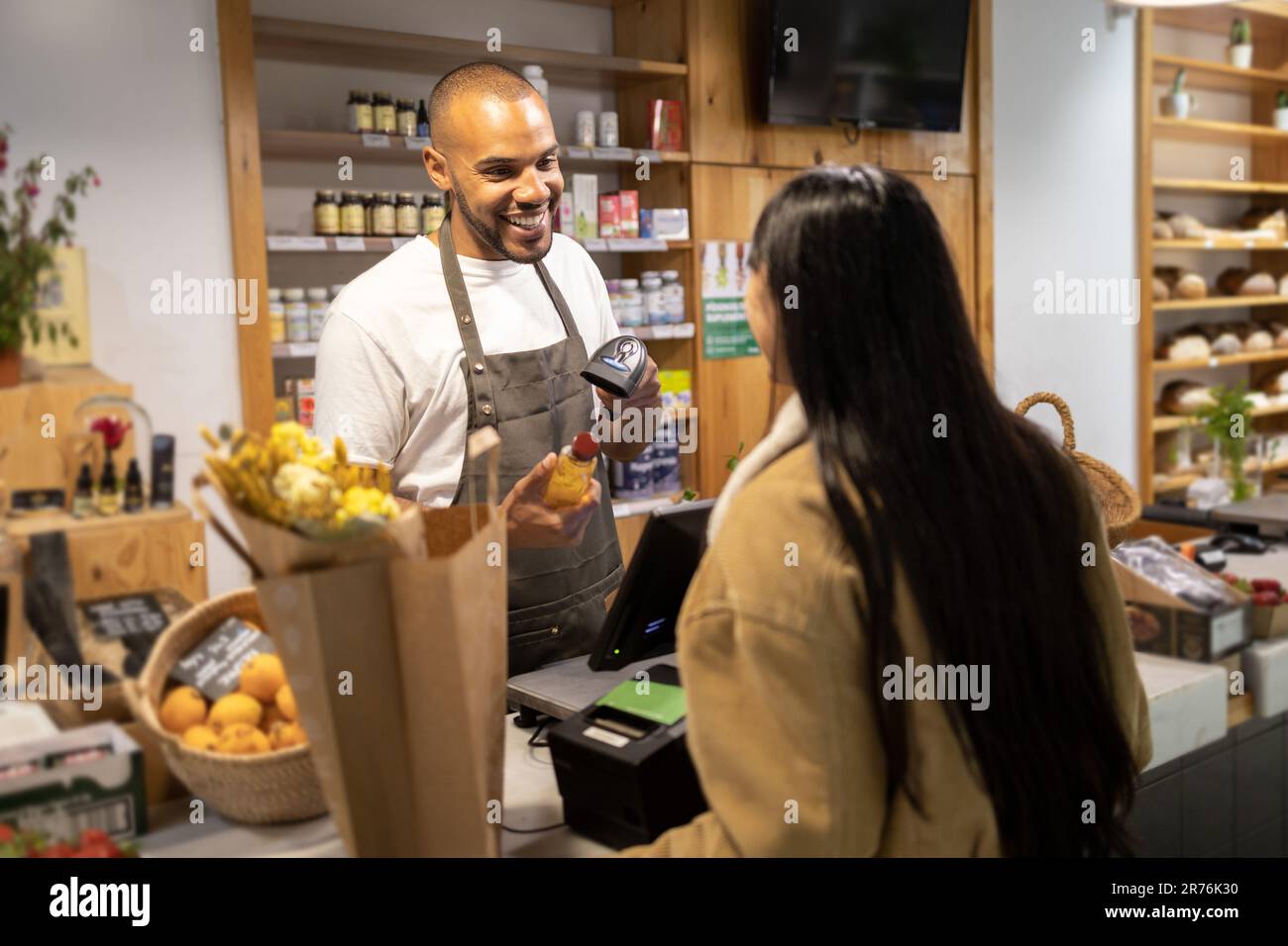 Cheerful African American male shopkeeper in apron standing at counter ...