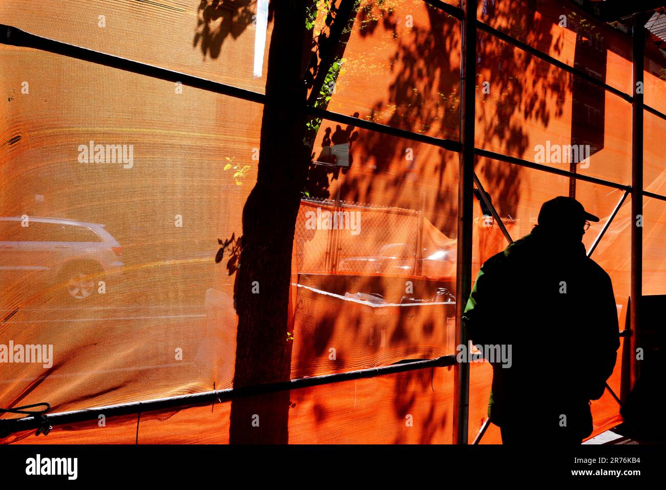 Silhouette of a figure against orange construction scrim under ...