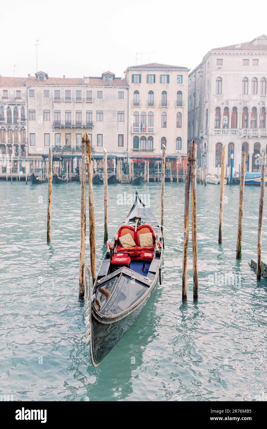 A single gondola floats in the canal in Venice. The seats are red and ...
