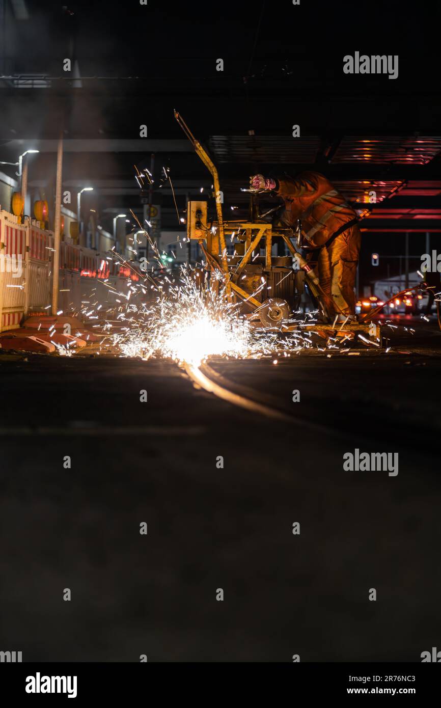 a construction worker cutting train tracks with a metal saw, sparks ...