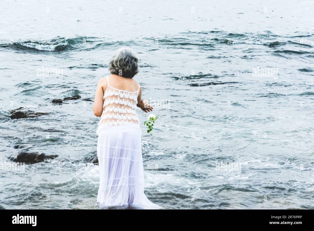 An elderly Caucasian woman is standing in the shallow waters of a rocky ...