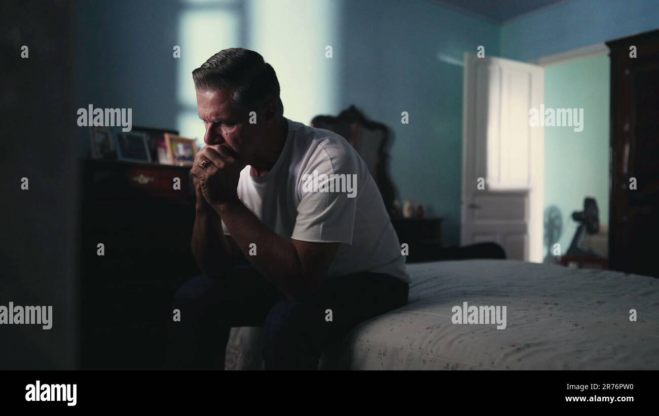 Contemplative older man sitting by bed pondering problems. Person in ...