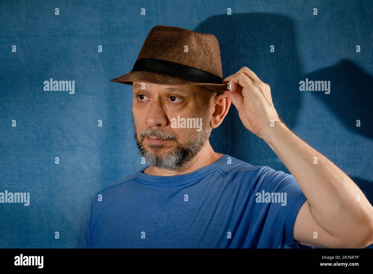 A young man tips his hat on a blue background Stock Photo - Alamy
