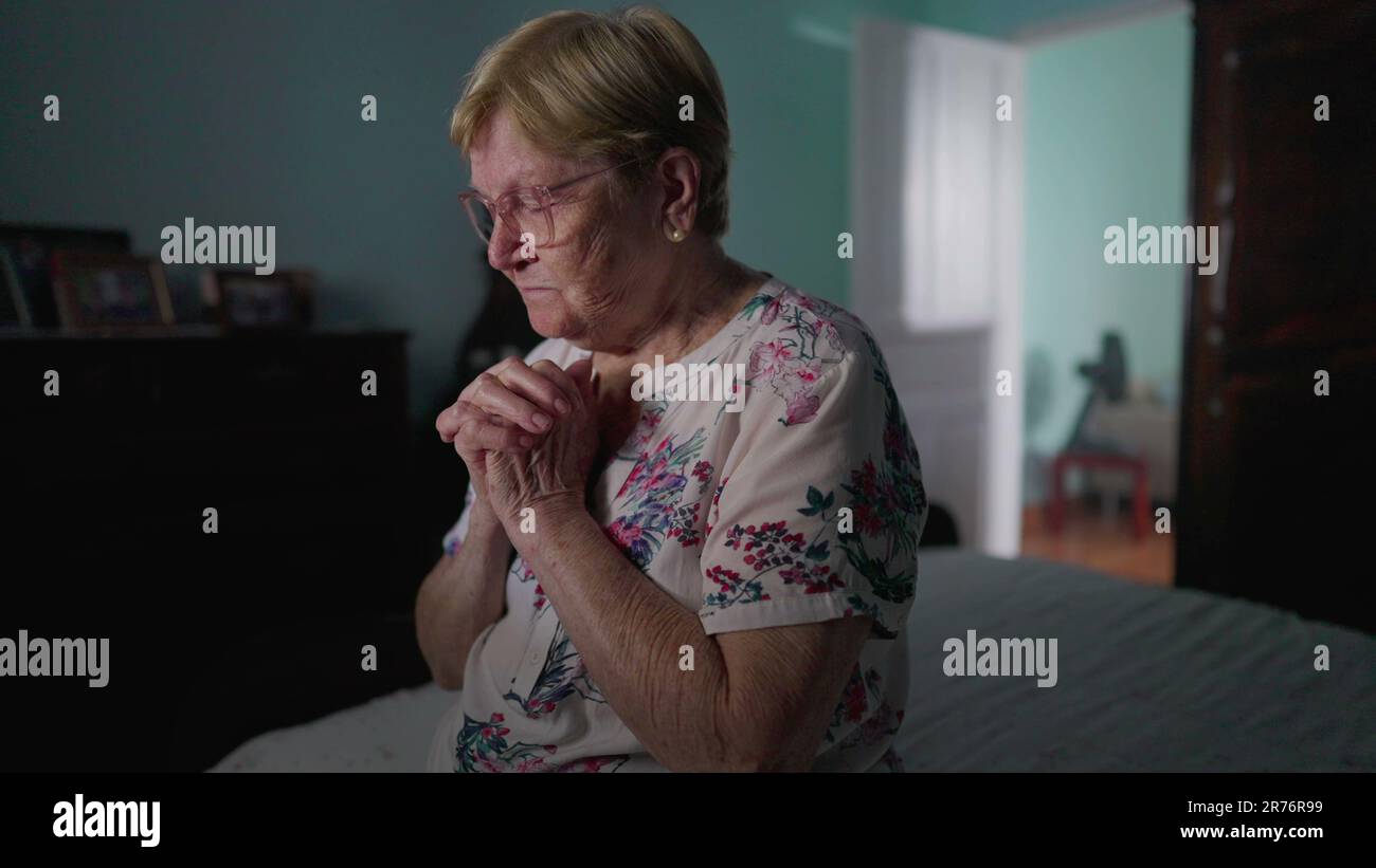 Religious Elderly woman sitting by bedside in Prayer. HOPEFUL older ...