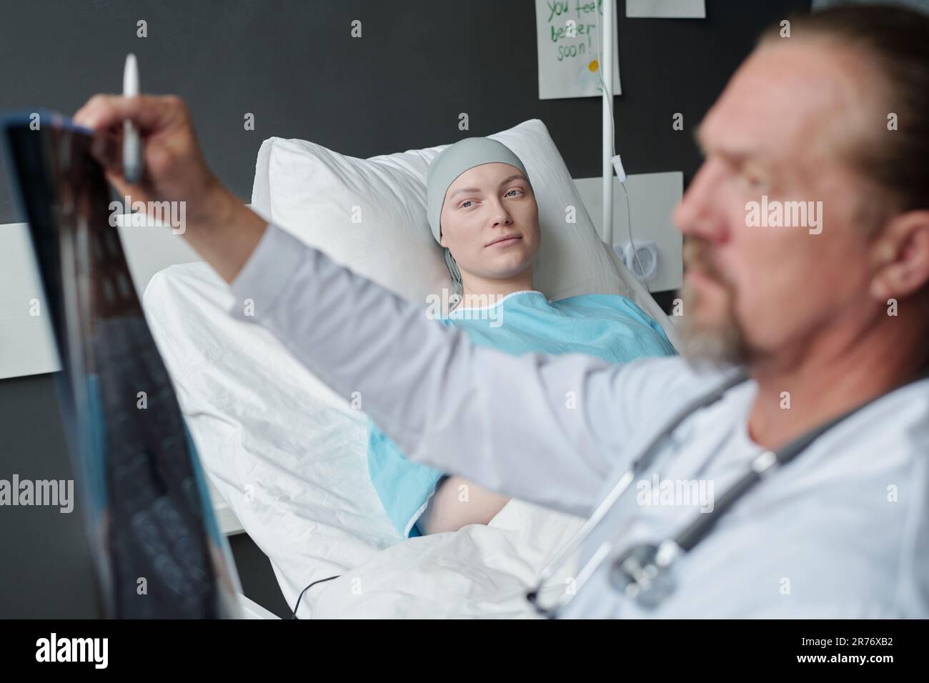 Young woman with brain cancer lying in bed and looking at oncologist ...