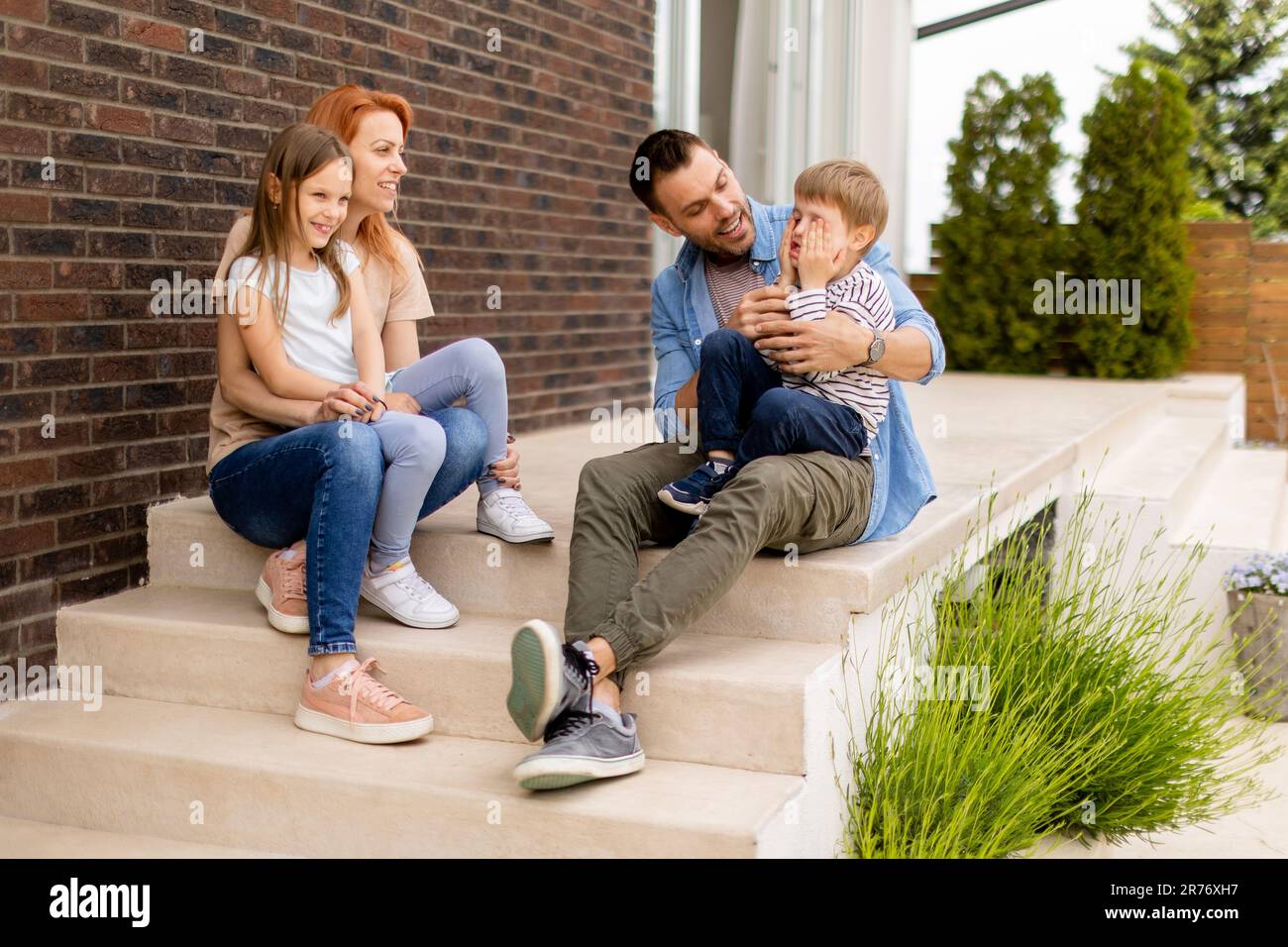 Family with a mother, father, son and daughter sitting outside on steps ...