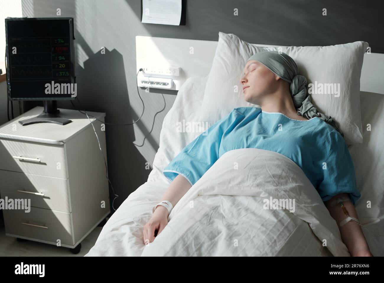 Young woman in headscarf sleeping under blanket in hospital bed next to ...