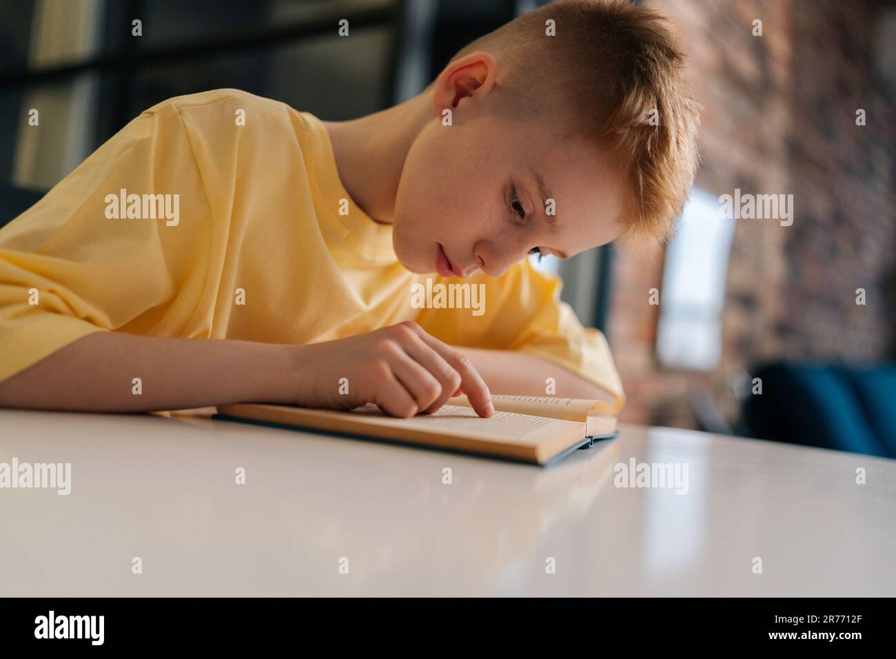 Close-up side view face of cute pupil schoolboy reading paper book ...