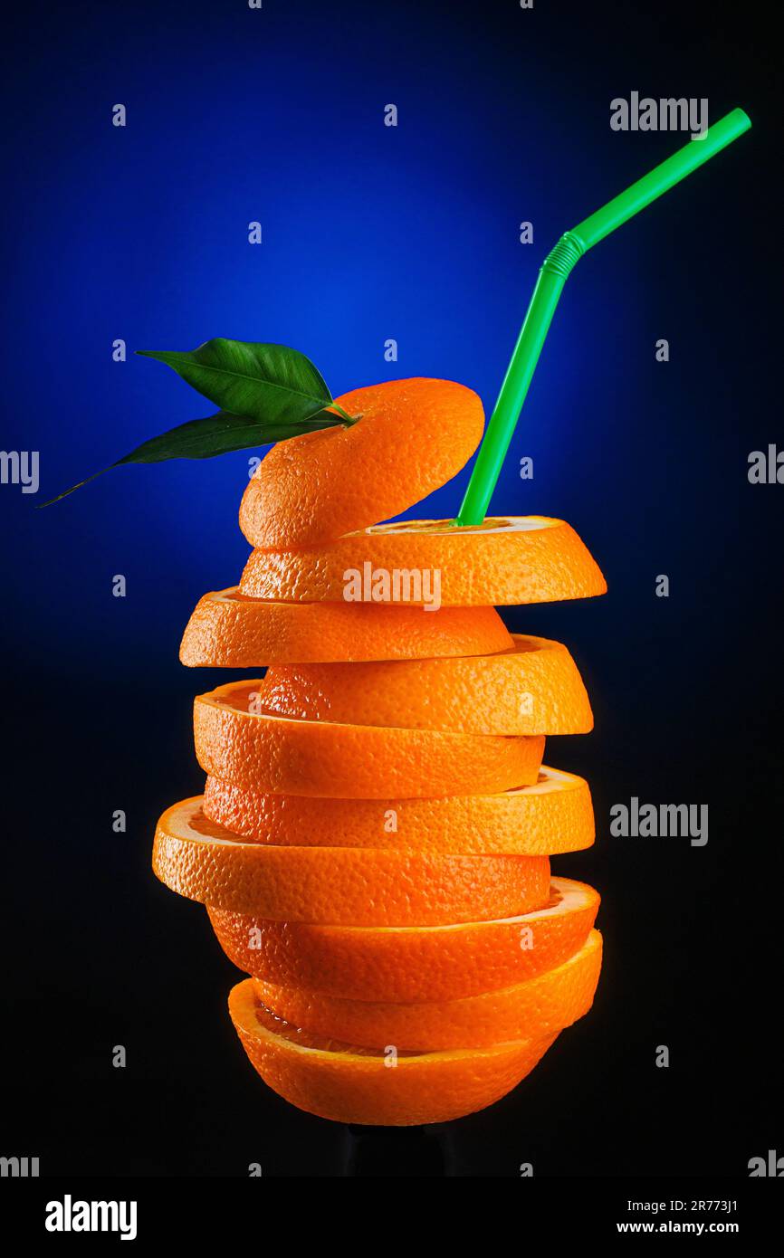 a stack of oranges with a green straw on a dark background with blue ...