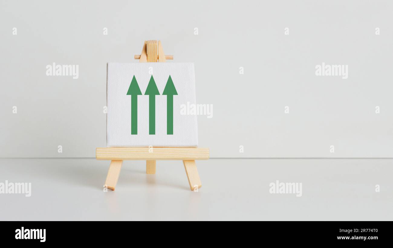A wooden easel with a green arrow pointing upwards against a plain ...