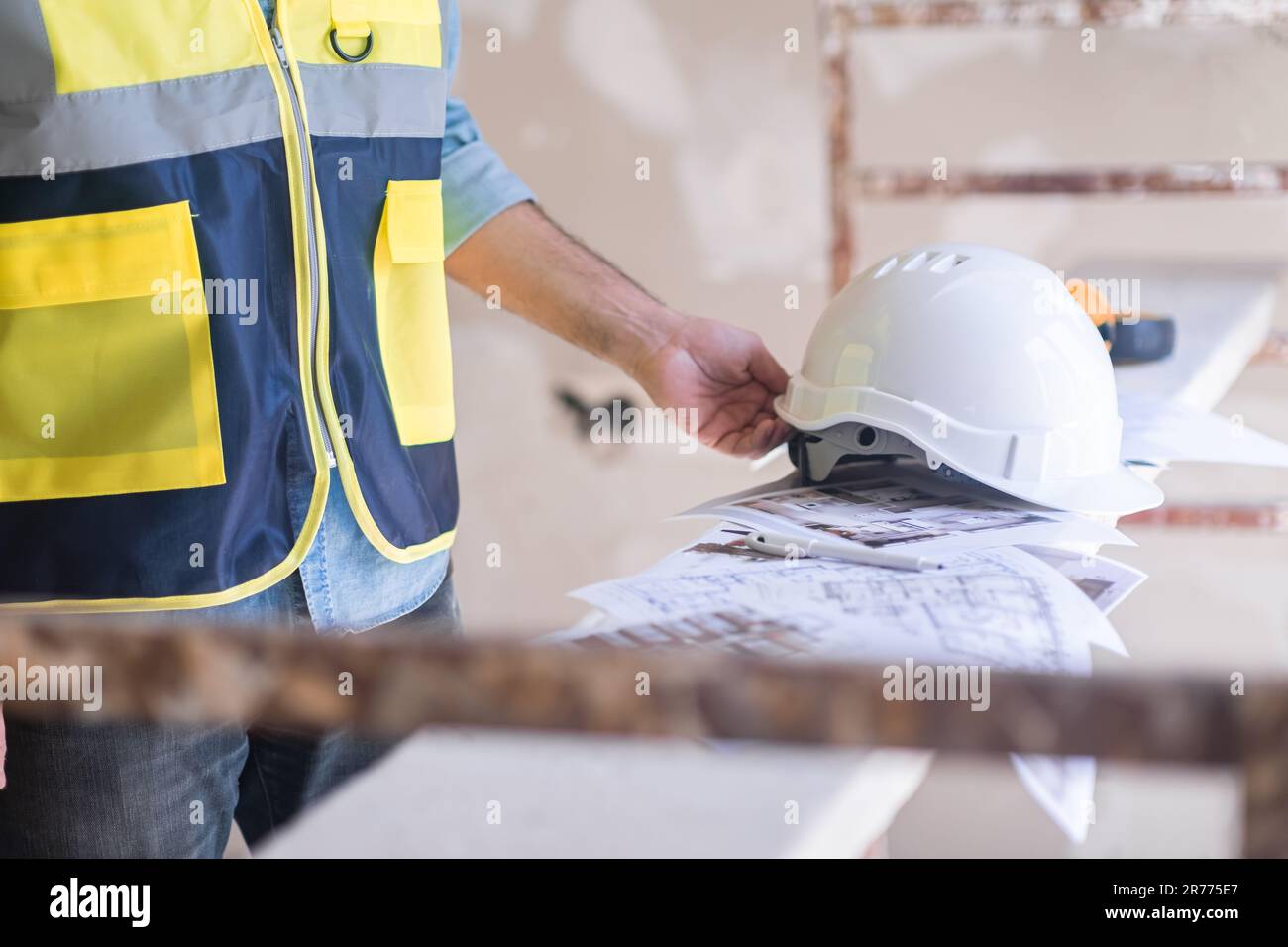 Architect in vest taking white helmet on heap of project papers to ...