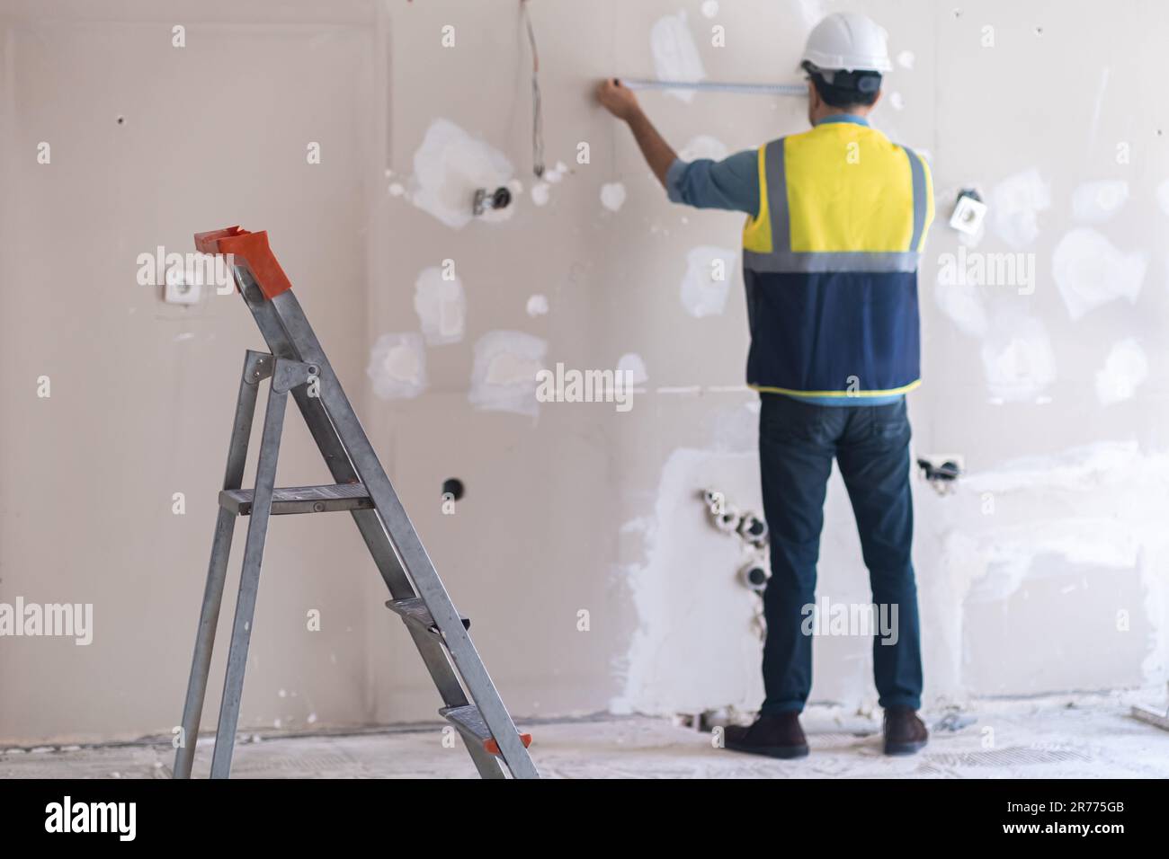 Skilled worker in professional uniform standing near ladder measures ...