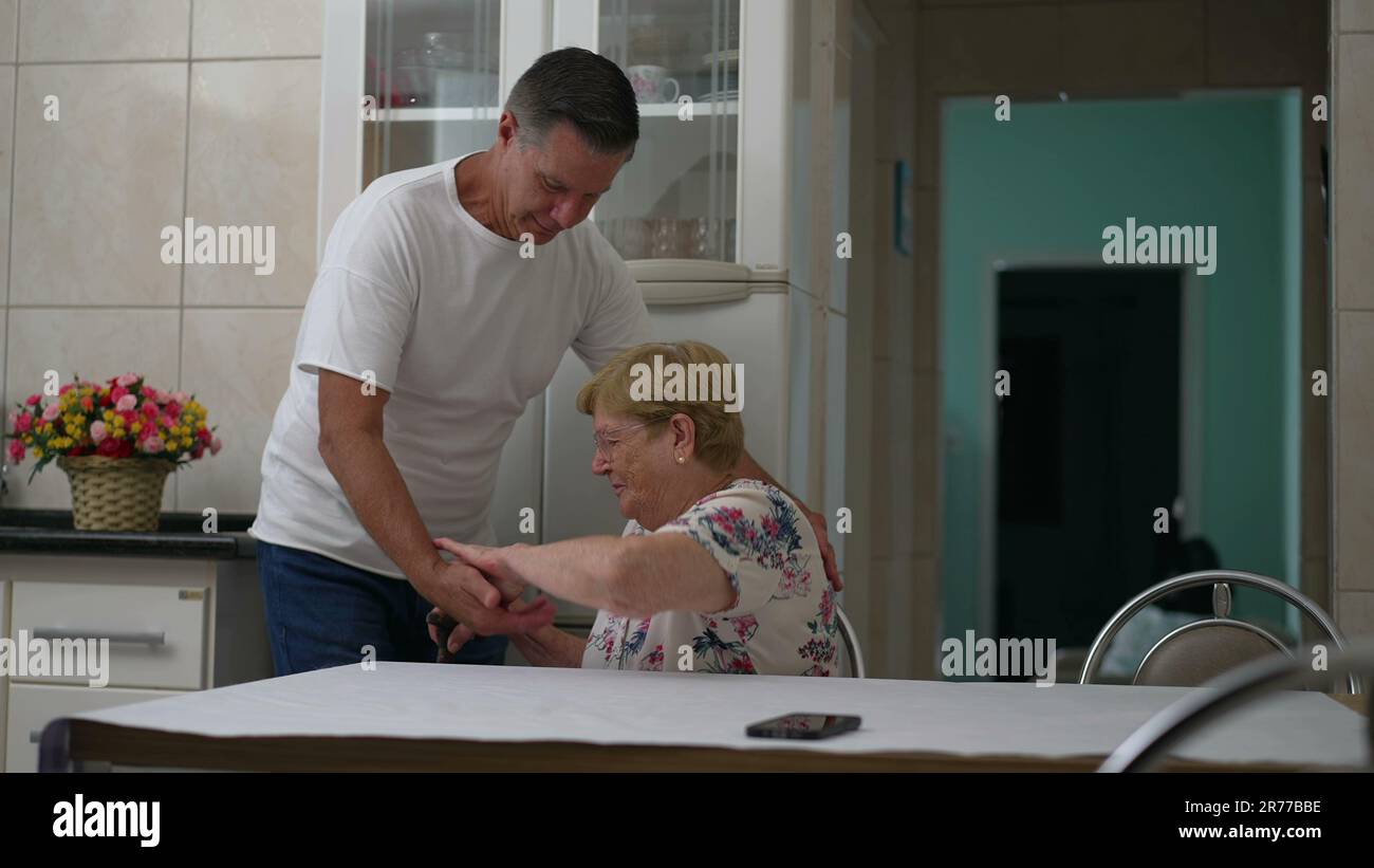 Caretaking moment of middle-aged son helping elderly mother get up from ...