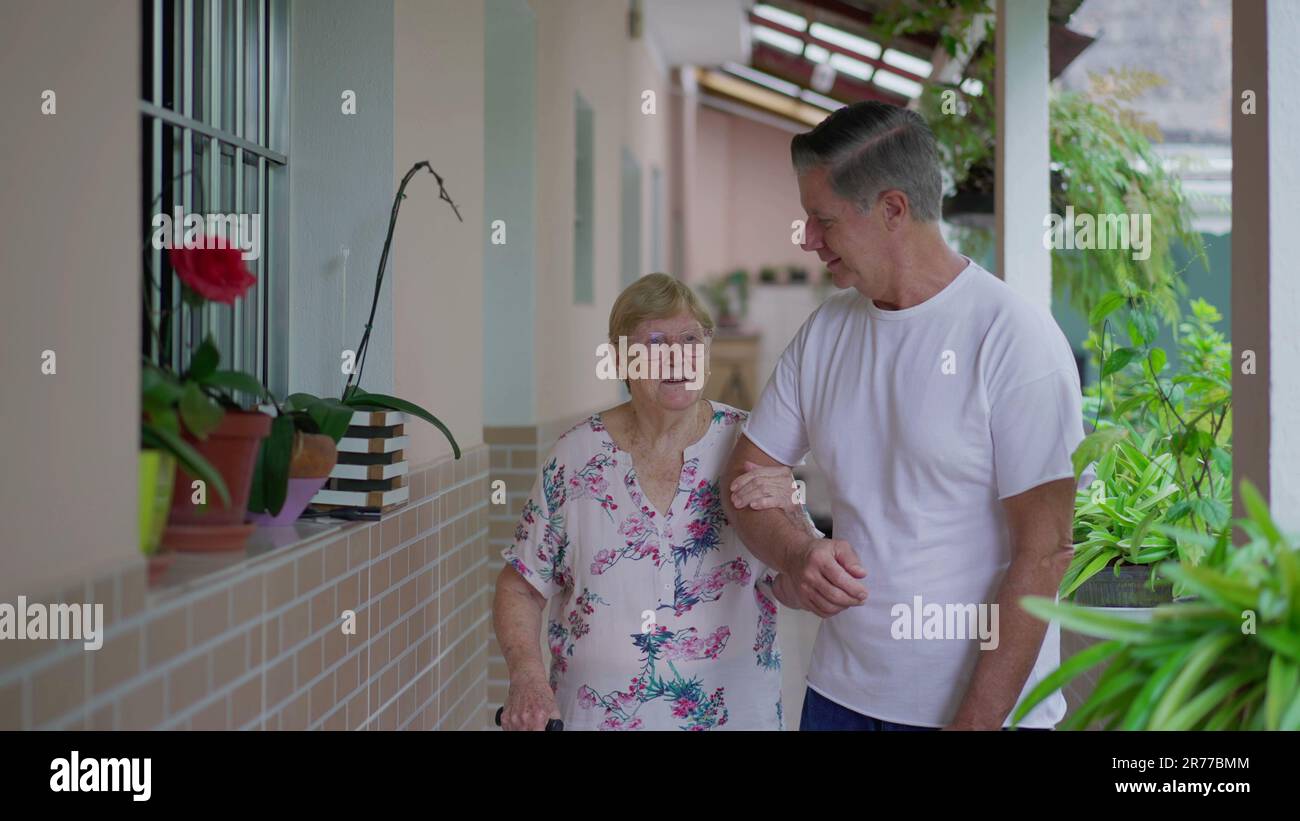 Adult son helping elderly mother to walk outside in home backyard ...