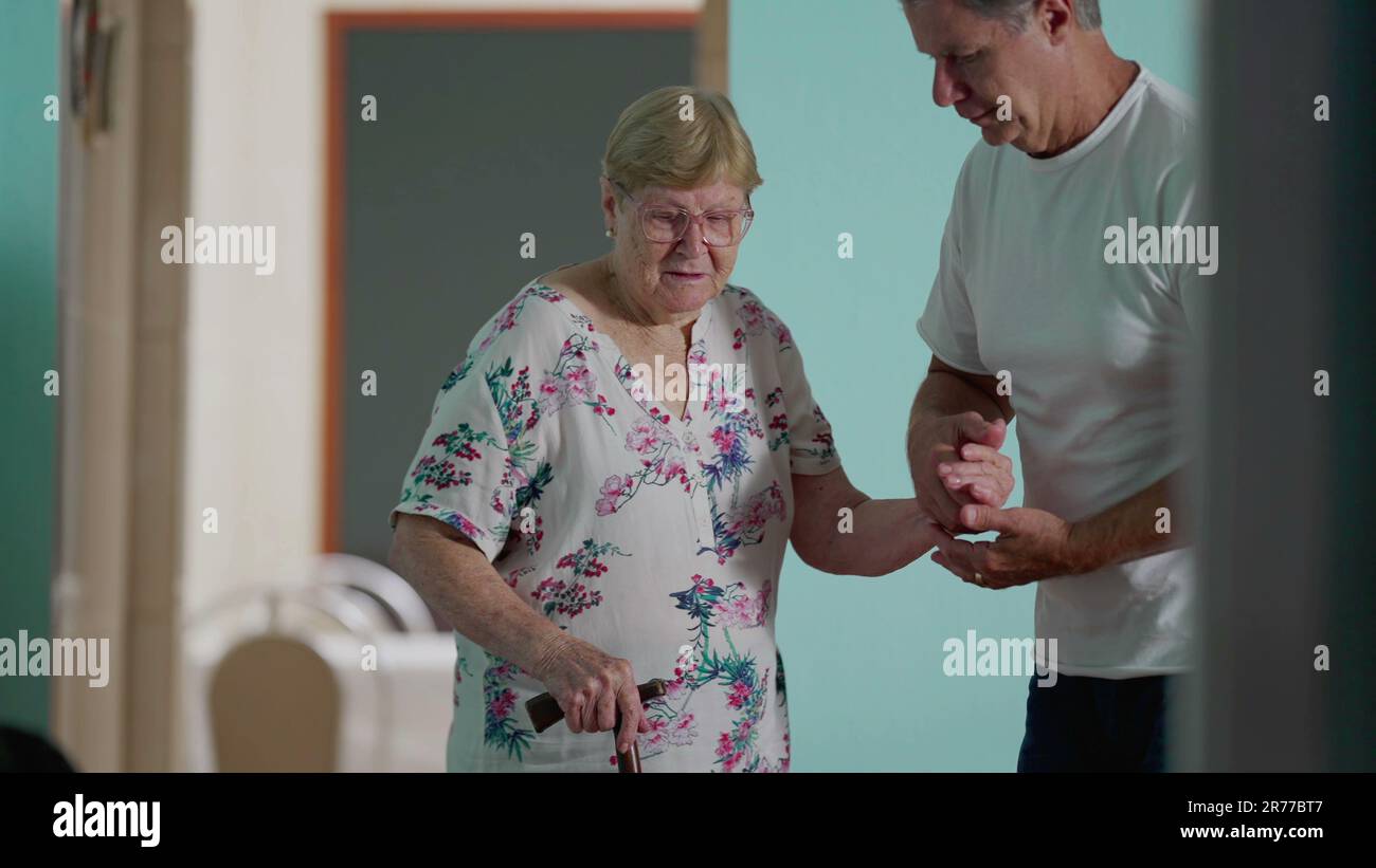 Assisting Elderly woman at home, candid authentic scene of adult son ...