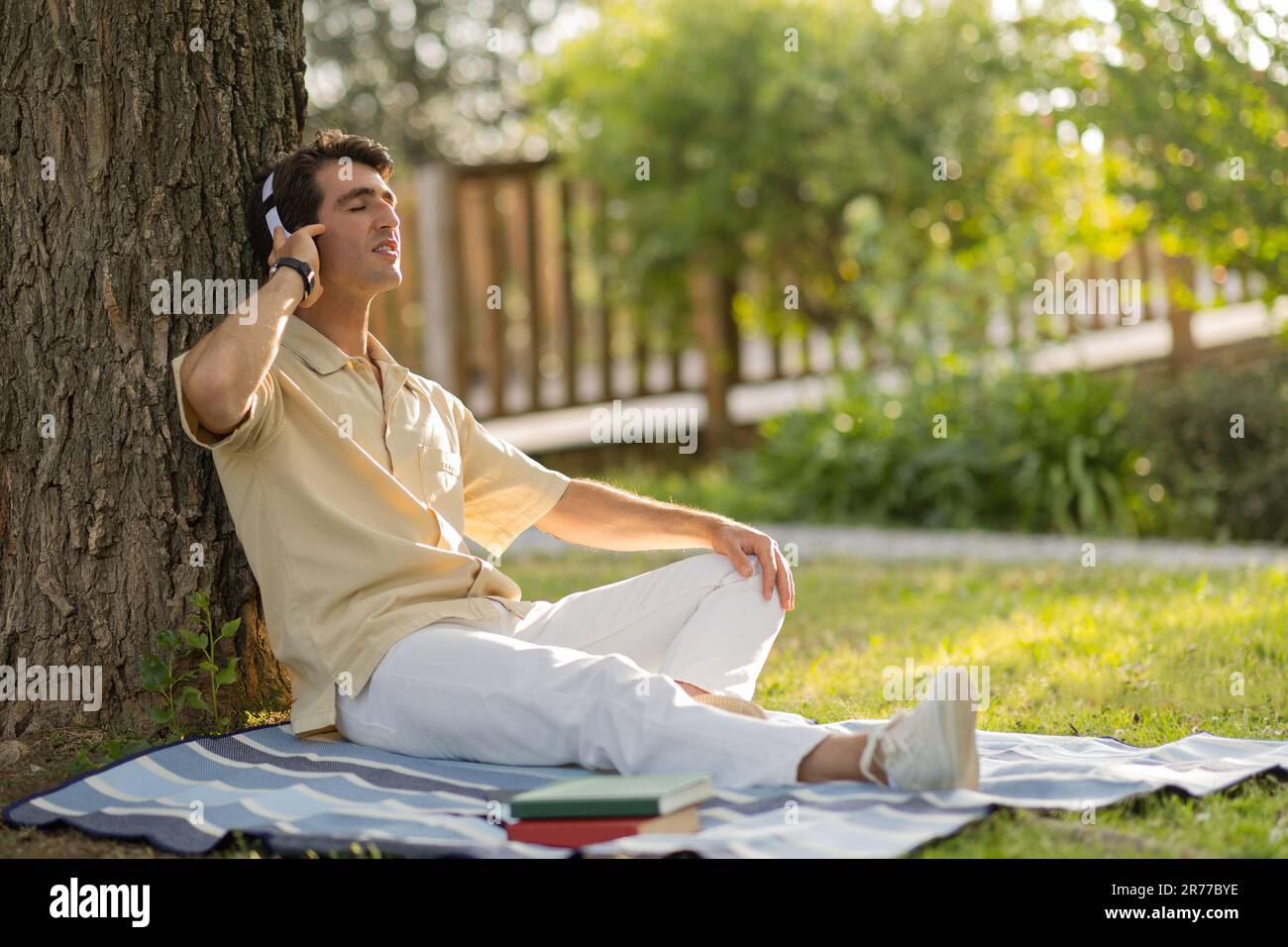 Relaxed young man sitting under tree, listening to music Stock Photo ...