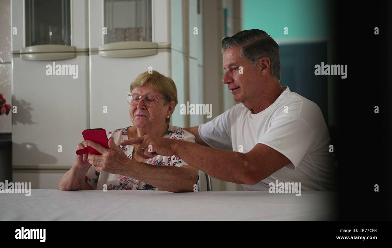 Candid Middle-Aged son helping elderly mother with modern technology in ...