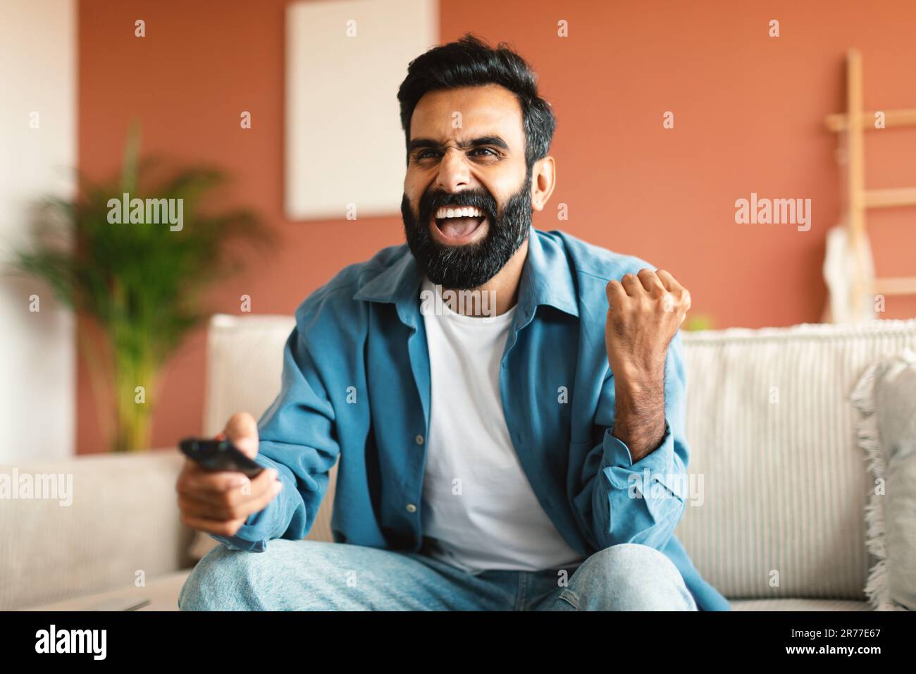 Joyful indian man shaking fists and shouting watching TV indoor Stock ...