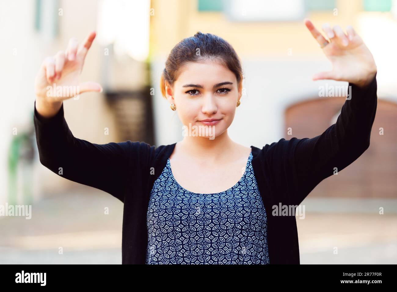 Outdoor portrait of young asian 20 year old girl focusing with hands ...