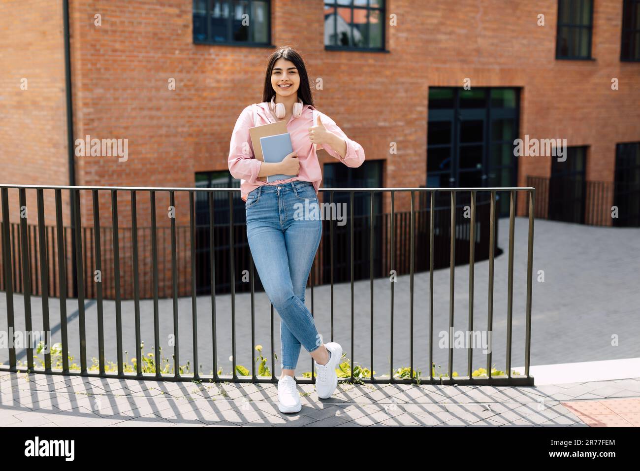 Happy hispanic student lady gesturing thumbs up and smiling, standing ...