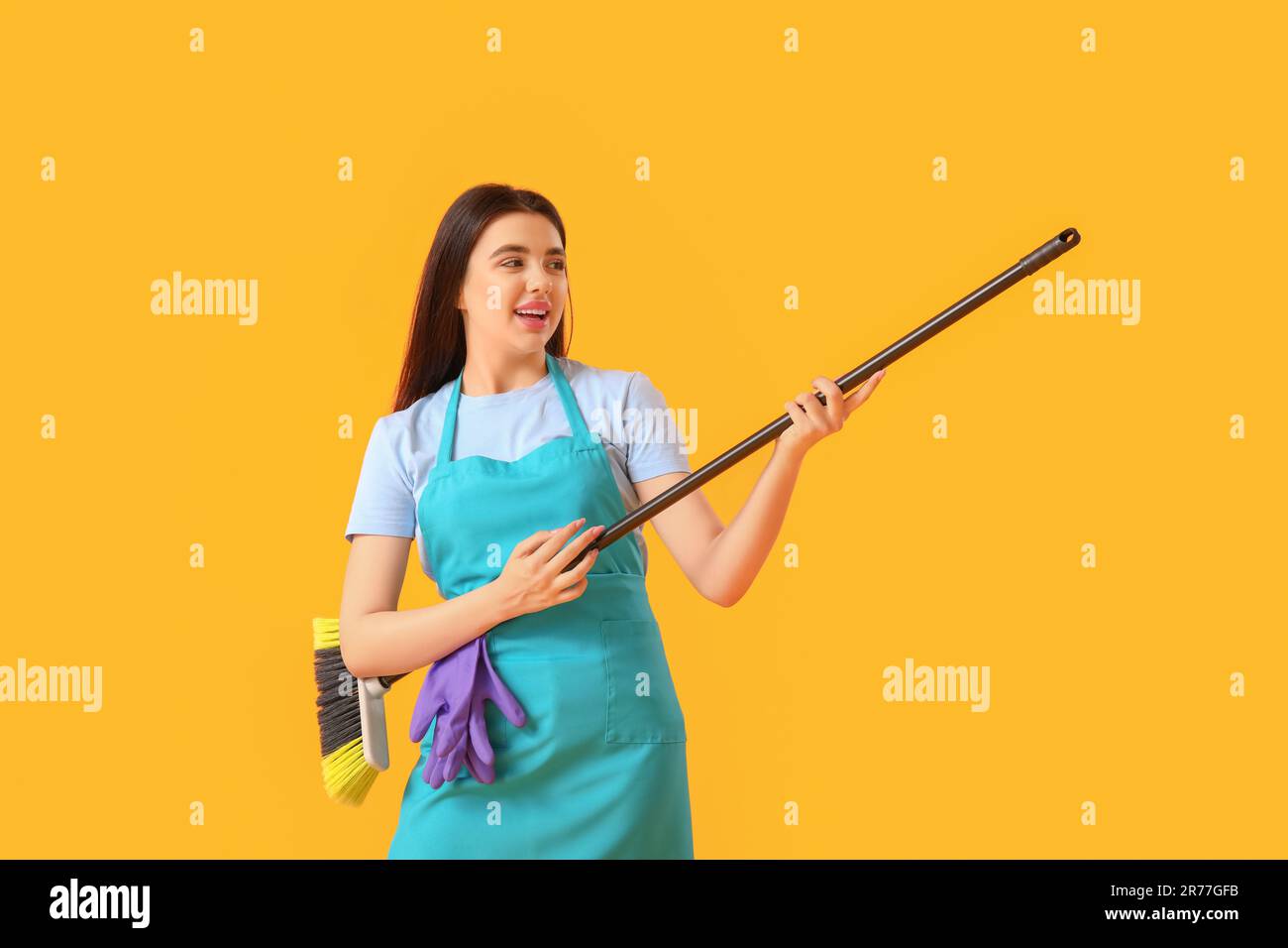 Female janitor with broom singing on yellow background Stock Photo - Alamy
