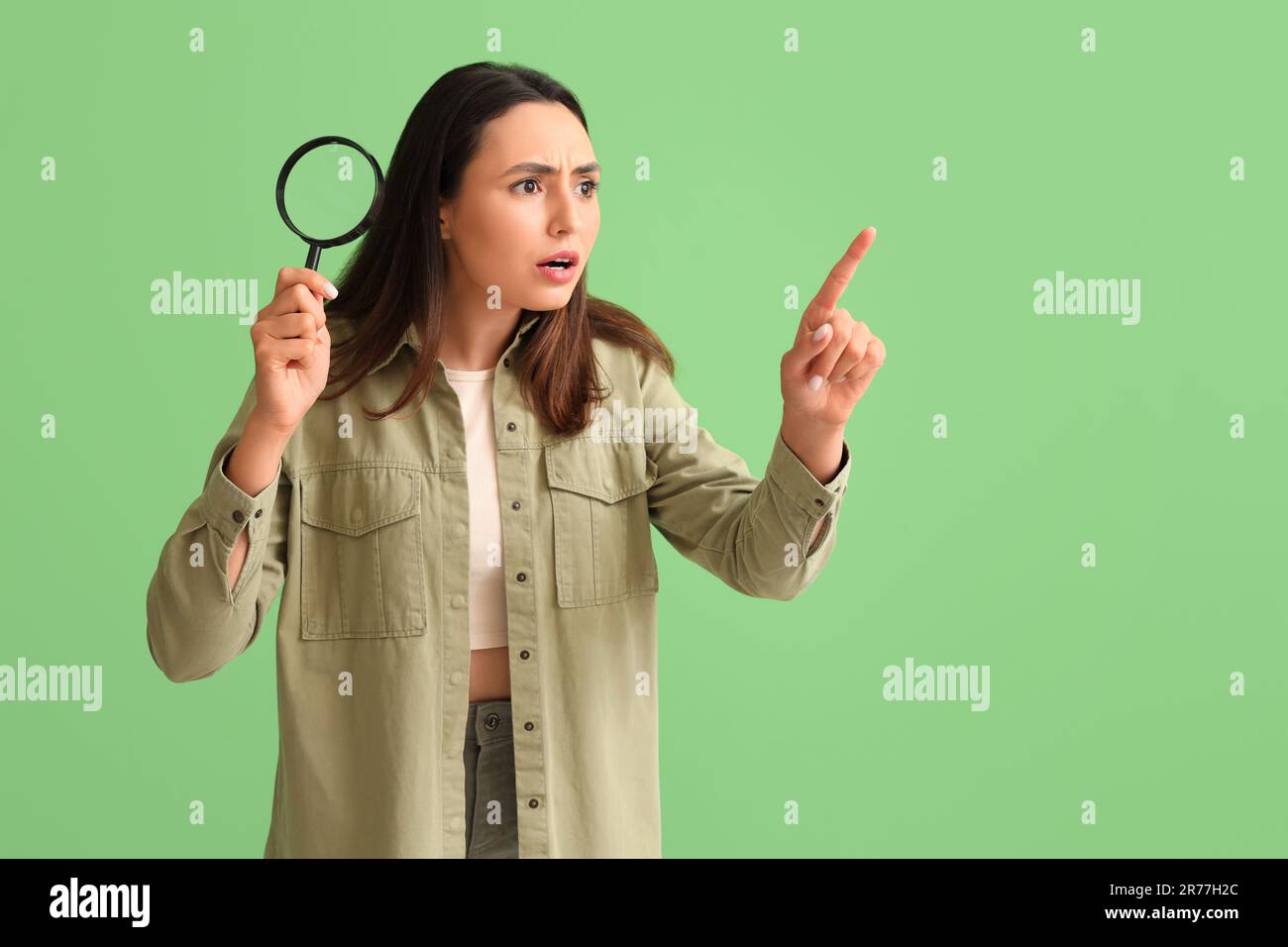 Shocked young woman with magnifier pointing at something on green ...