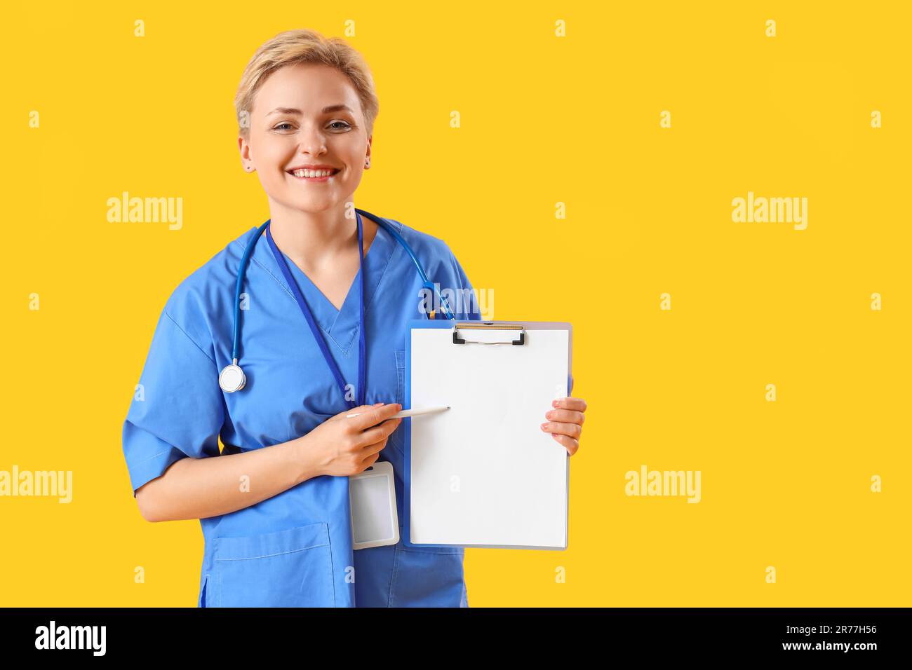 Female medical intern pointing at clipboard on yellow background Stock ...