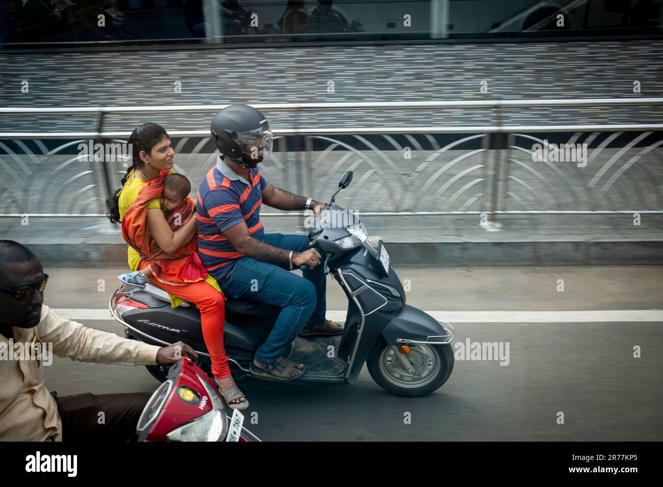 A mother holds baby tightly as father drive scooter through heavy ...