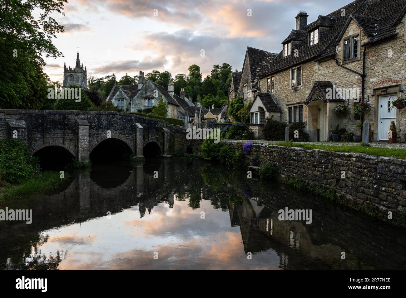The sun sets over the quaint Cotswold stone cottages and arch bridge of ...